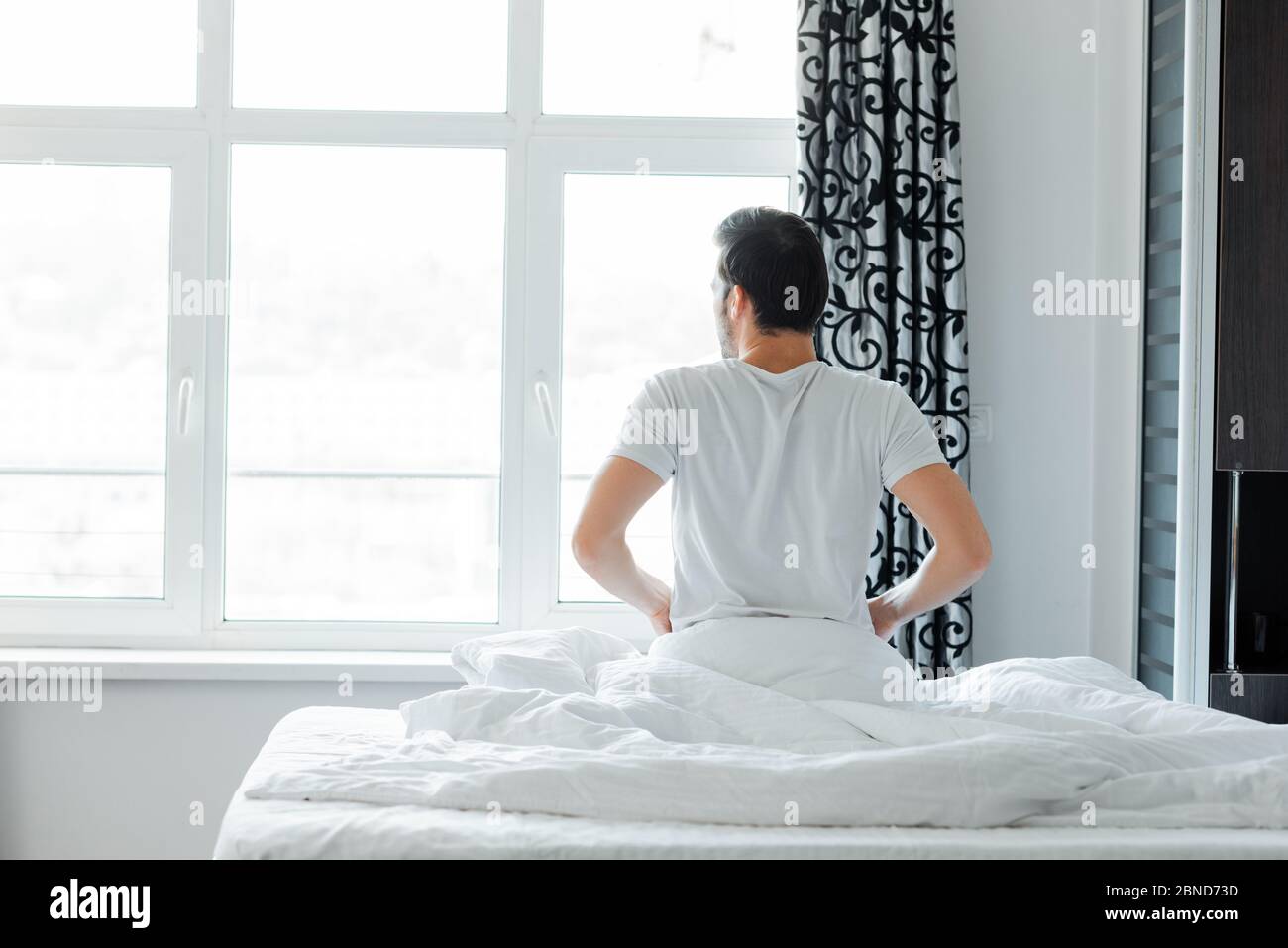 Back view of man looking at window while sitting on bed at home Stock ...