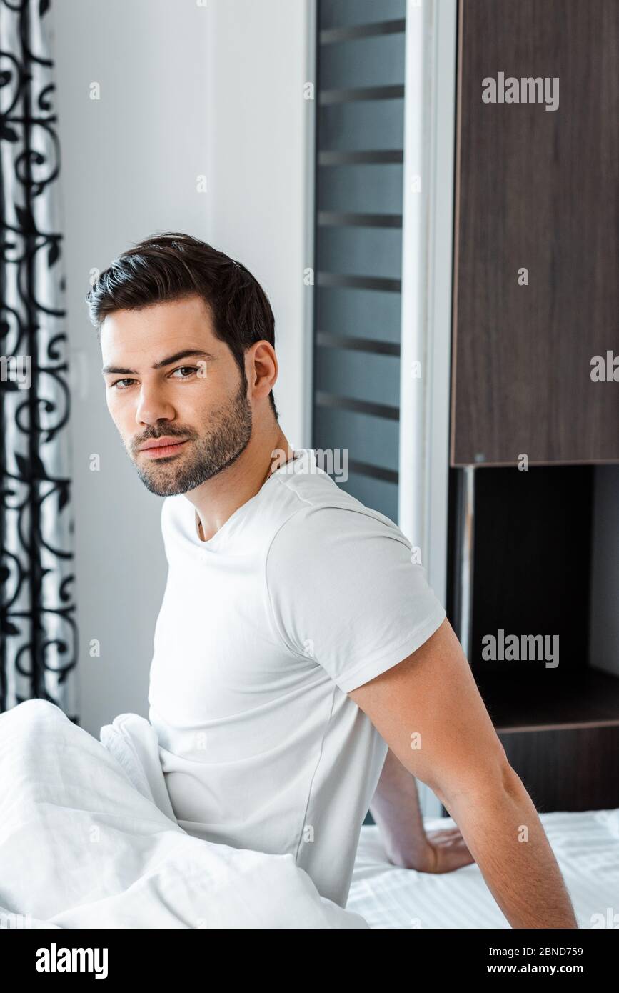 Side view of handsome man looking at camera while sitting on bed Stock ...