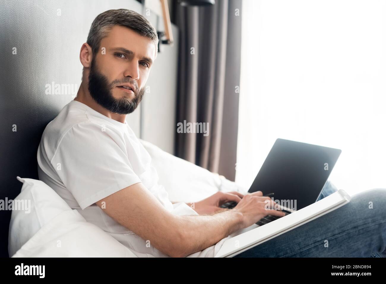 Side view of handsome freelancer looking at camera while using laptop ...
