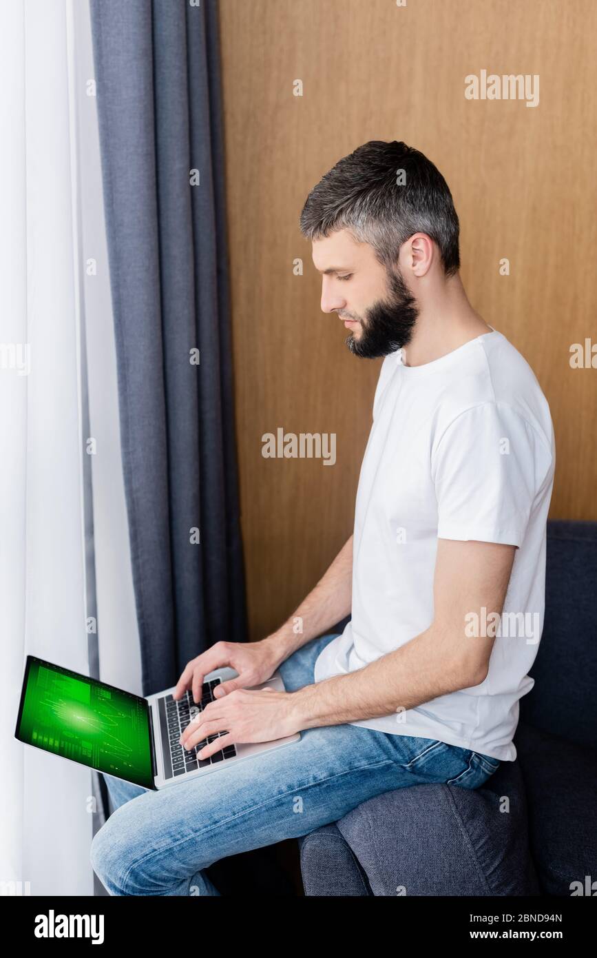 Side view of man using laptop with charts and graphs on screen in ...