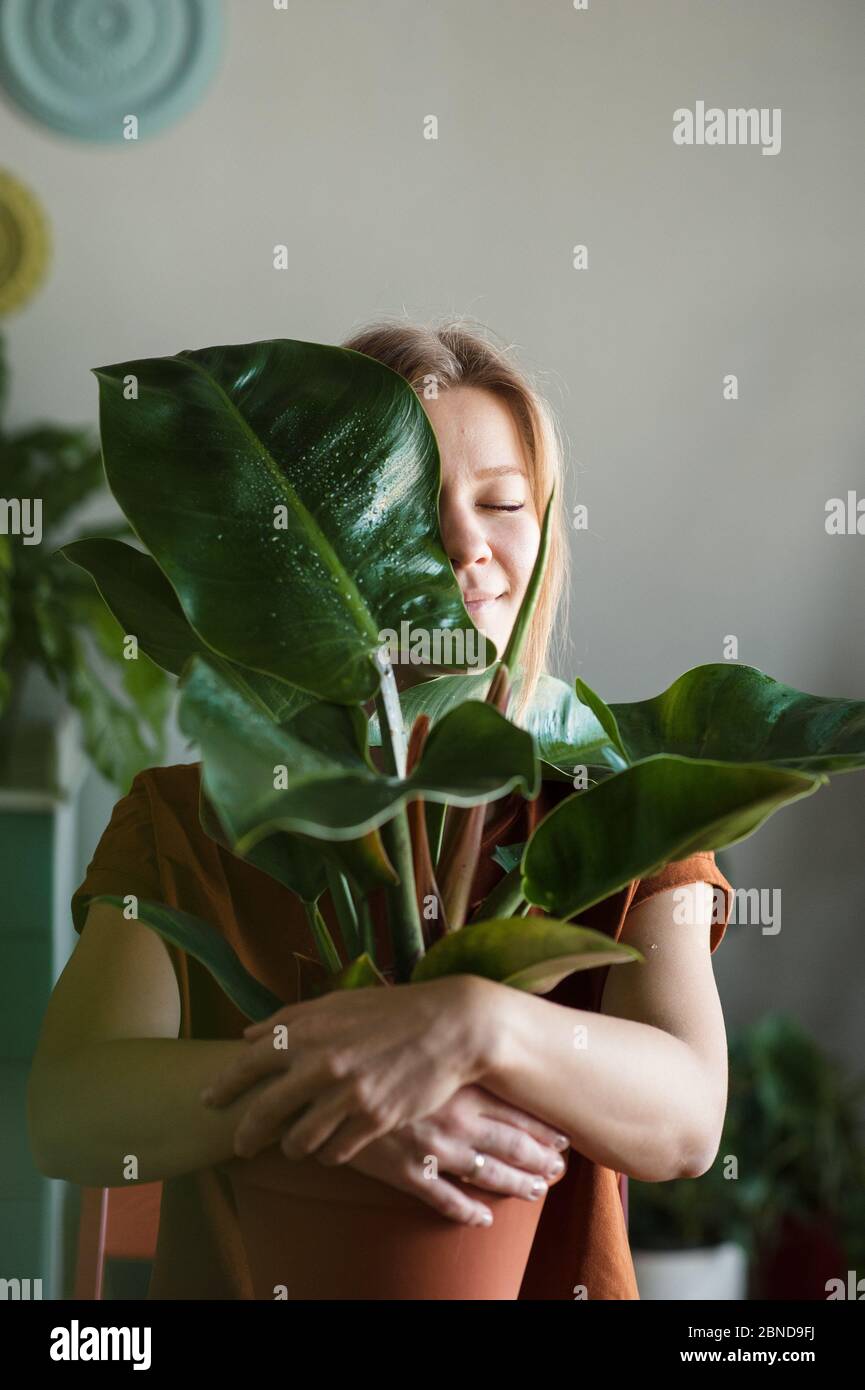 Woman hugs potted plant with big leaf wich closes her half of face ...