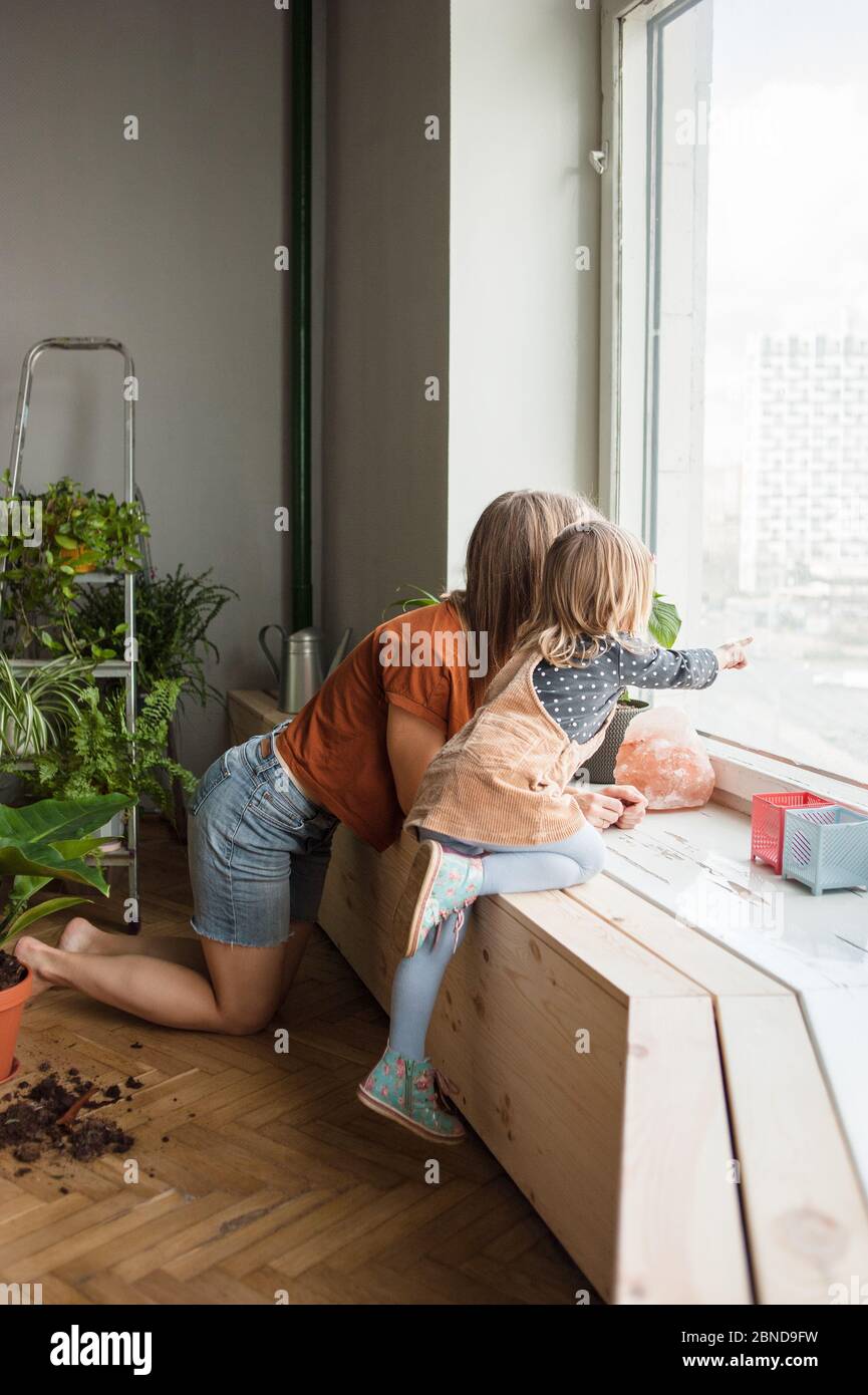 Mother and daughter look outside kneeling at window. Kid points Stock ...