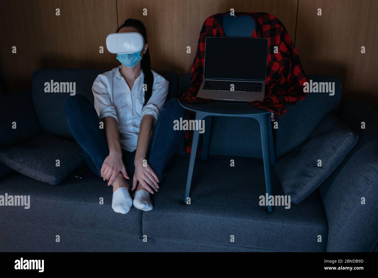 depressed woman sitting on sofa and using vr headset near laptop with ...