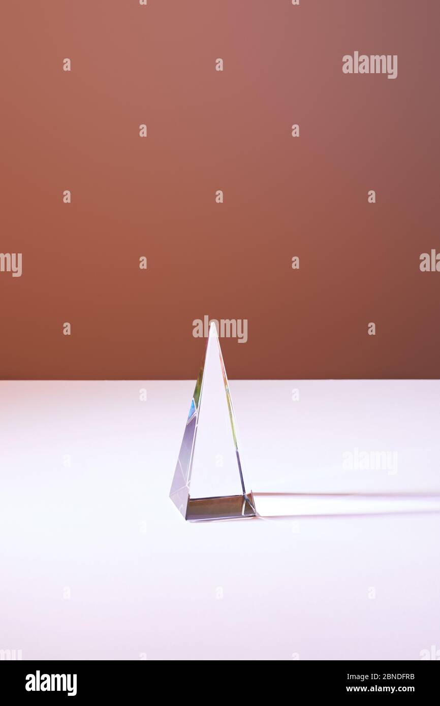 crystal transparent pyramid with light reflection on brown background ...