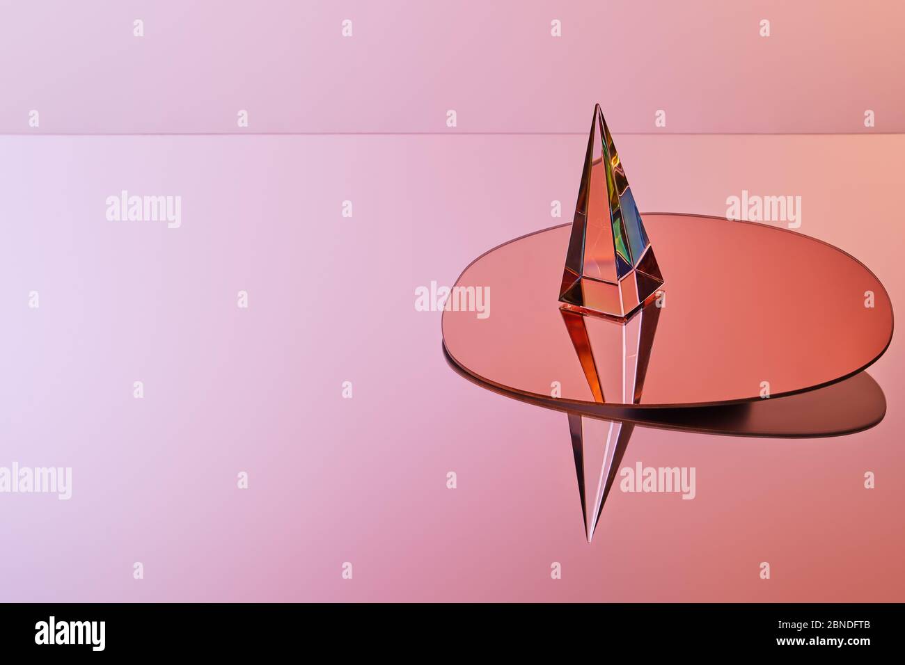 crystal transparent pyramid with reflection on round mirror on pink ...