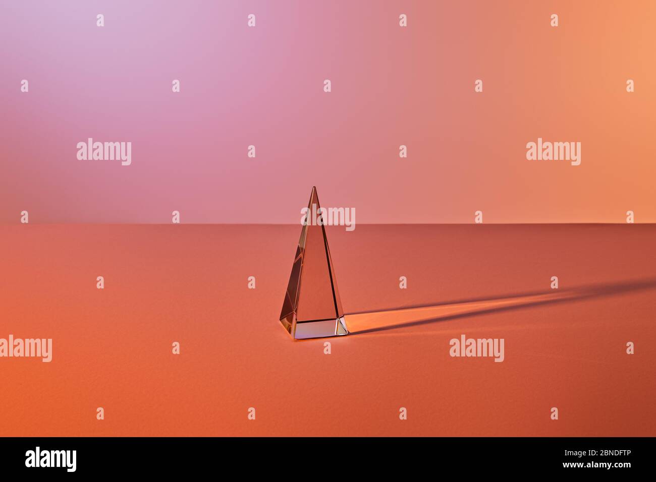 crystal transparent pyramid with light reflection on orange background ...