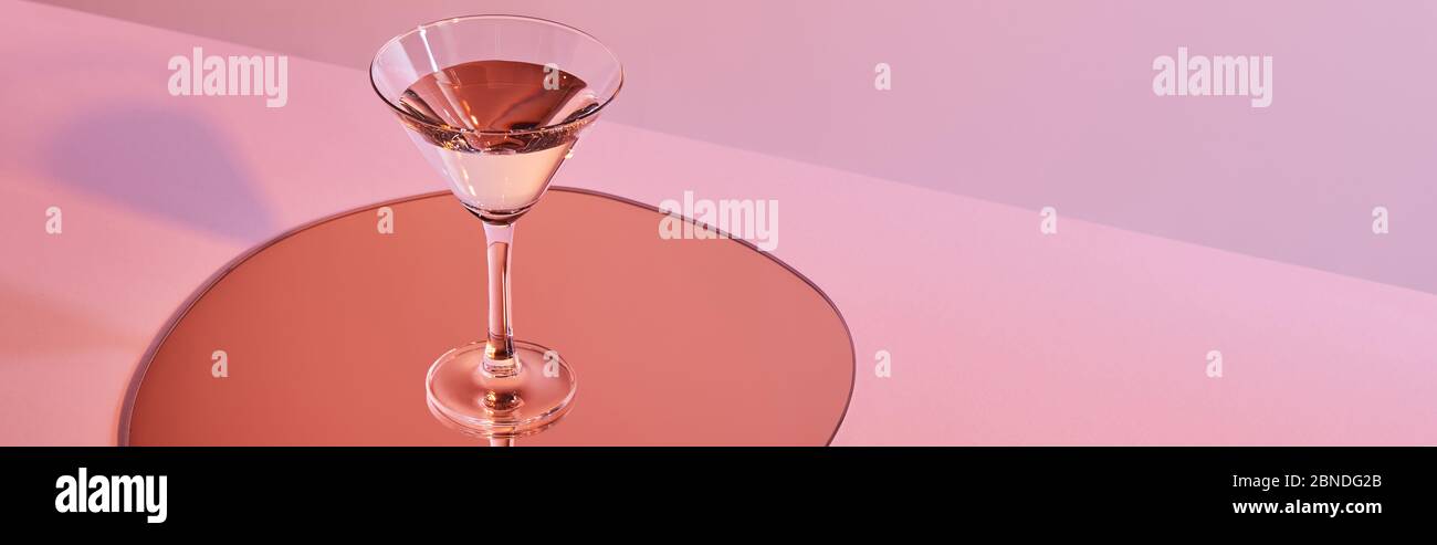 cocktail glass with liquid on mirror with reflection on pink background ...