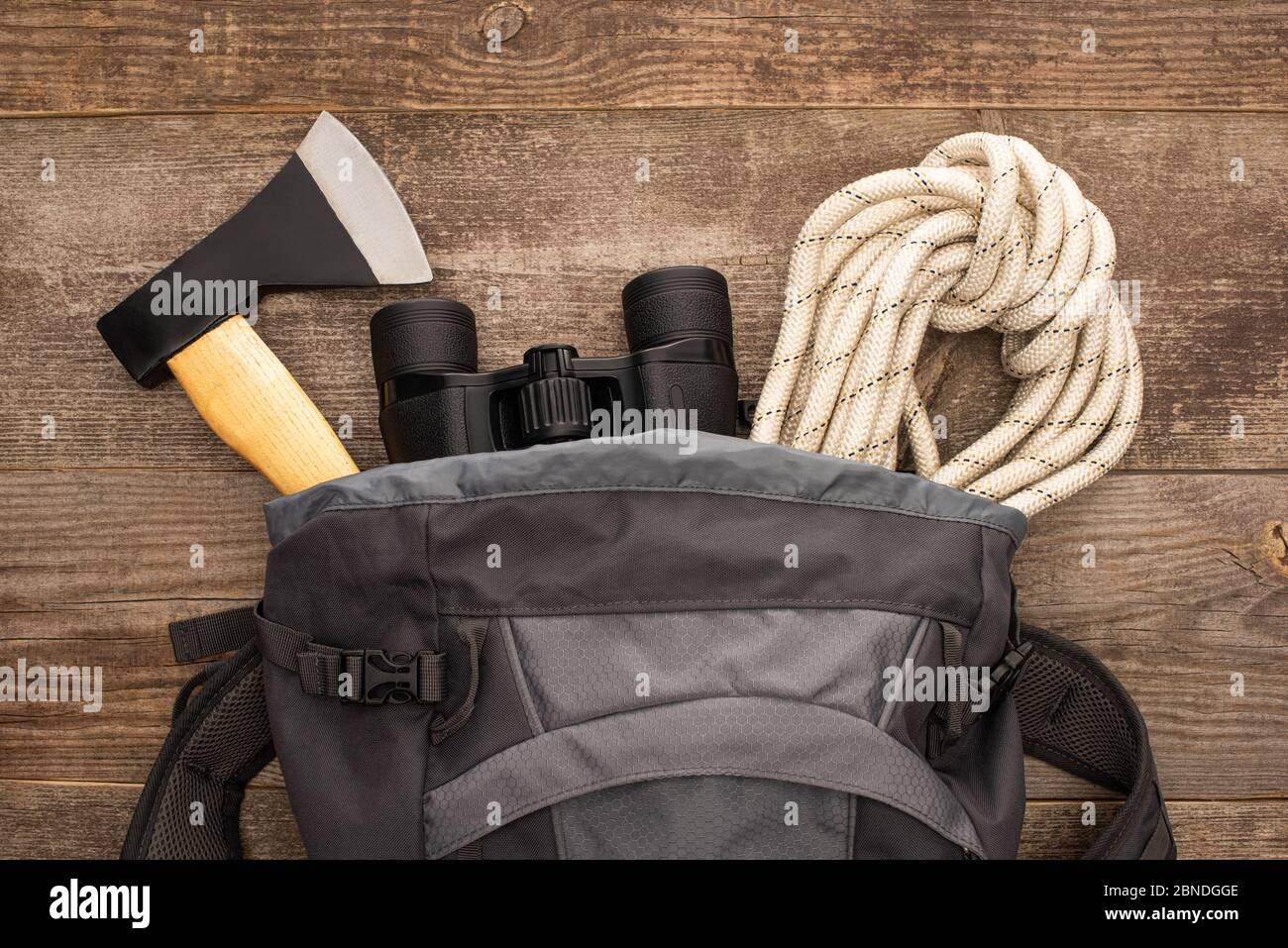 top view of backpack with axe, hiking rope and binoculars on wooden ...
