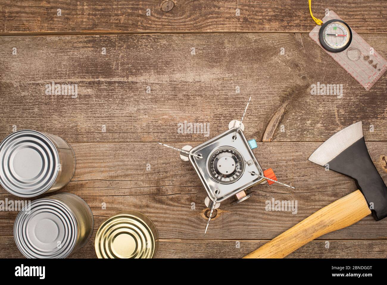 top view of gas burner, axe, compass and canned goods on wooden surface ...