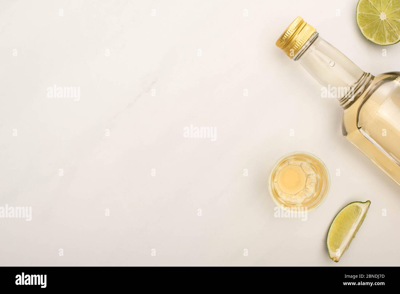 top view of golden tequila in bottle and shot glass with lime on white ...