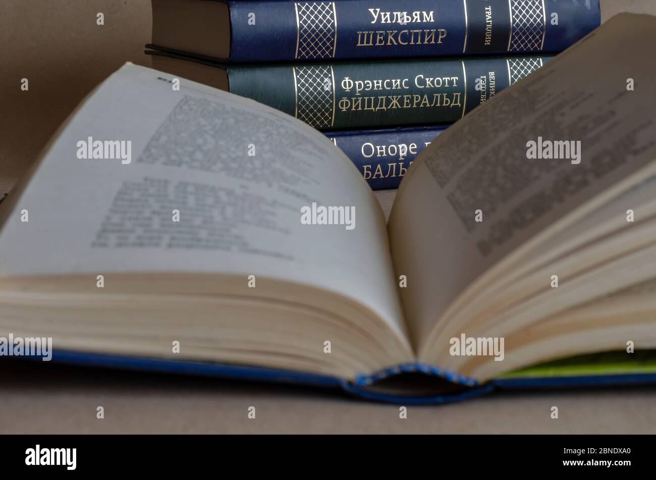An open book on a table in a library. In the background is a stack of ...