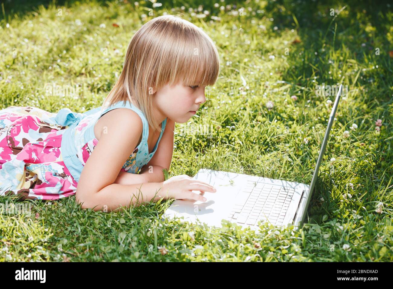 Little girl using laptop computer in a backyard. Child studying at home ...
