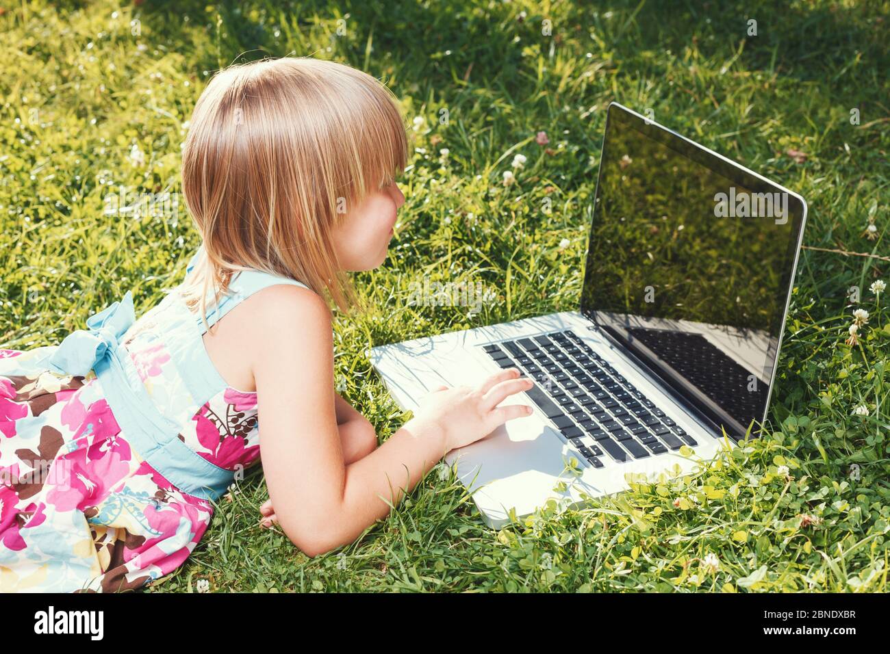 Little girl using laptop computer in a backyard. Child studying at home ...