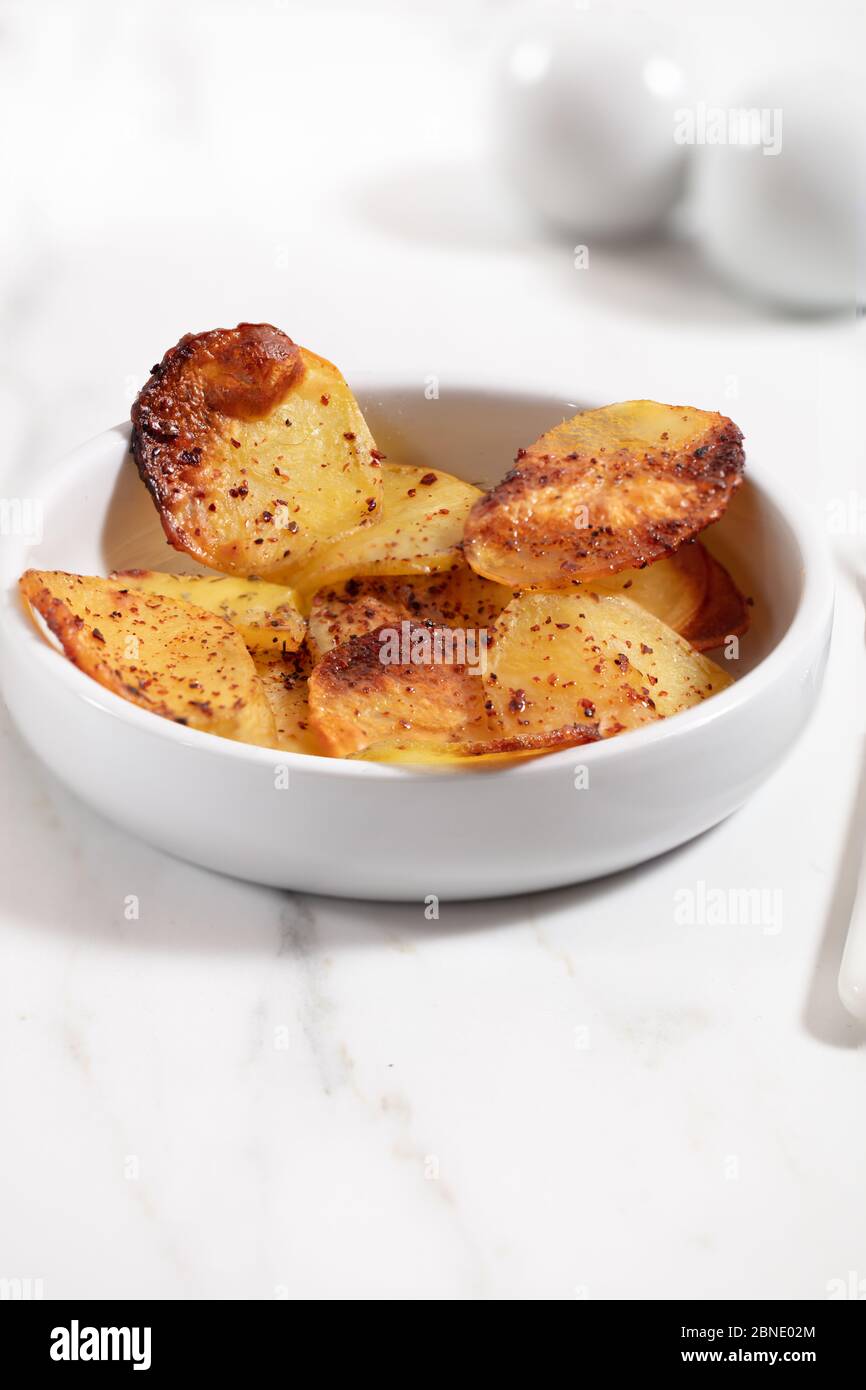 Slices of the round spicy baked potatoes in a white plate on a table ...