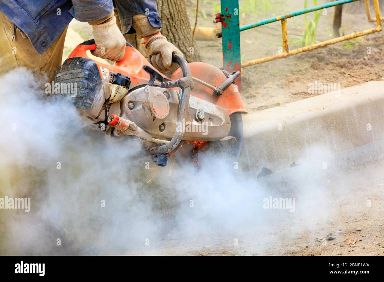 A worker using a portable concrete cutter and cutting a diamond blade ...