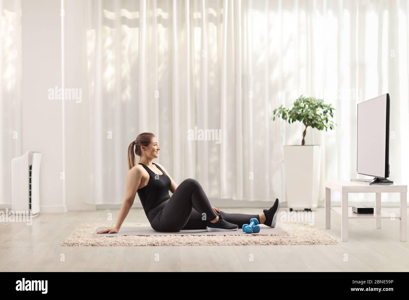 Full length profile shot of a young woman sitting on an exercise mat ...