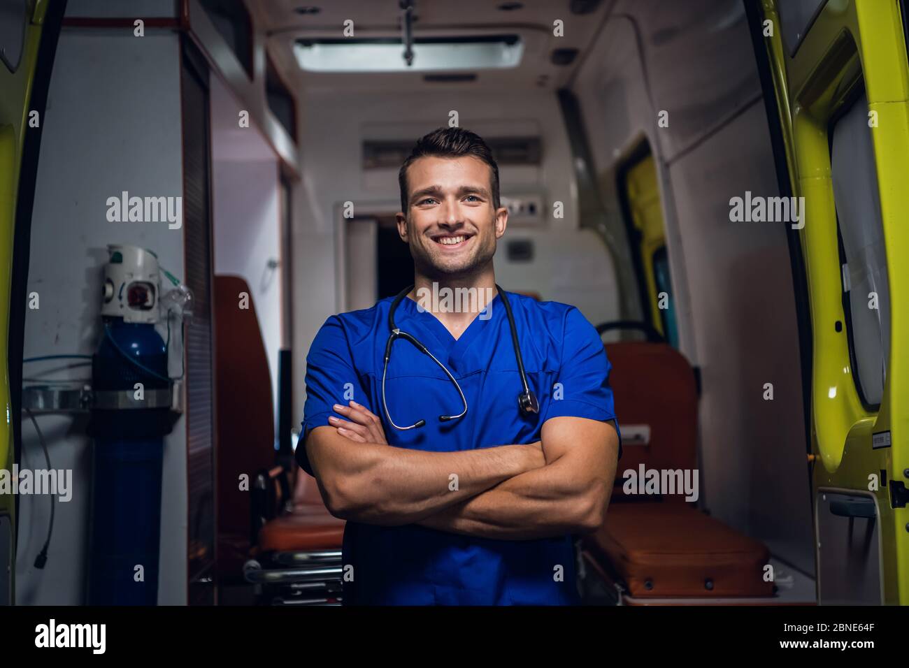 A portrait of a young male paramedic standing in front of an ambulance ...