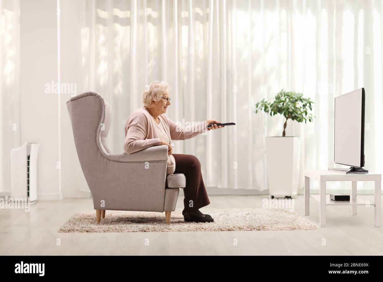 Elderly woman in an armchair changing channels on TV with remote ...