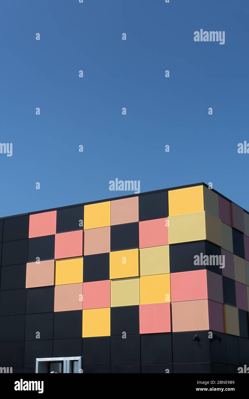 Matt black cubic building with yellow and red tiles in one corner as ...