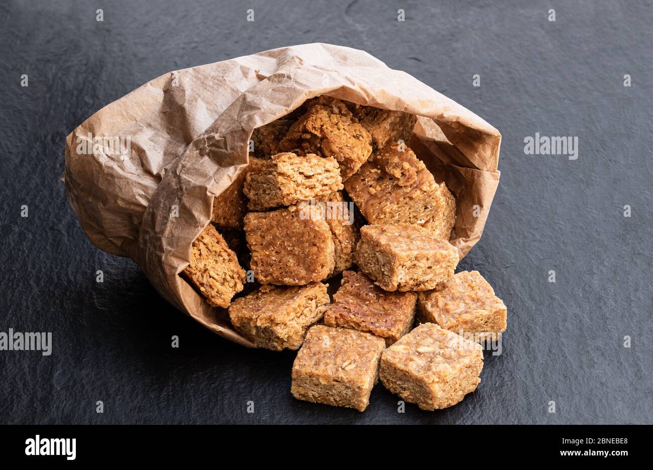 Mini oat and syrup flapjack slices in paper bag on black stone ...