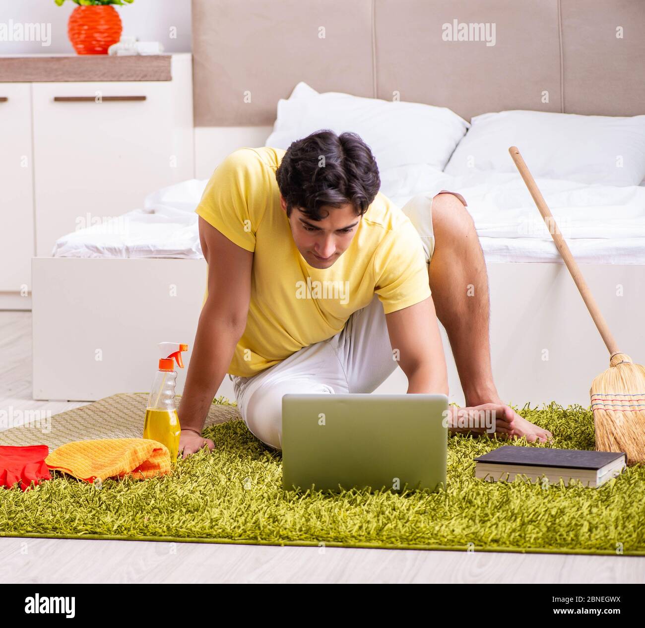 Young handsome man cleaning the bedroom and sitting at the computer ...