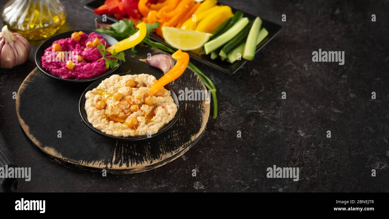 Variety of vegan hummus dips with colorful vegetable sticks on black ...