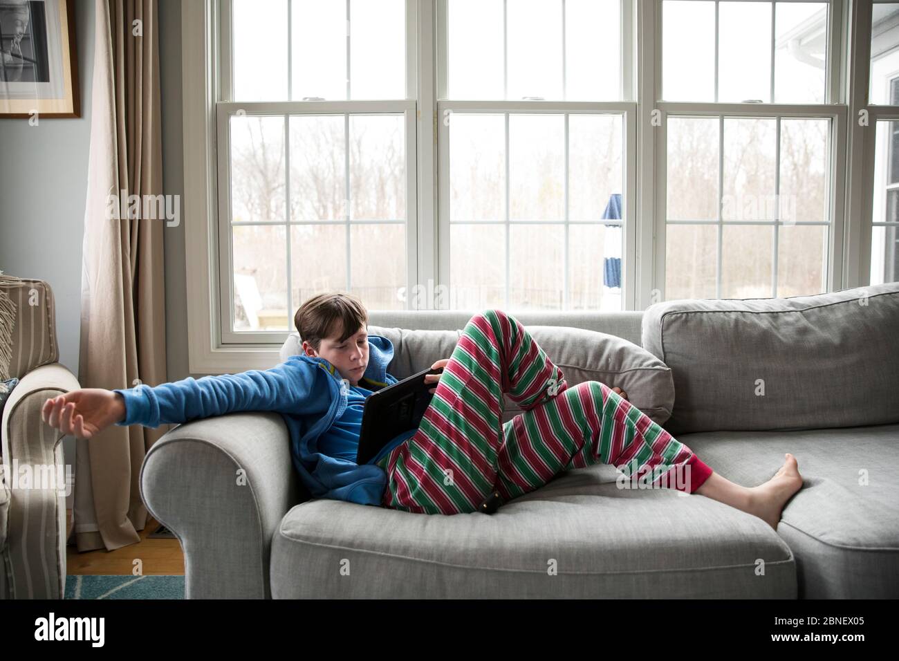 Teenage Boy With Flu, in Striped Pajamas, Sits on Couch Watching Ipad ...