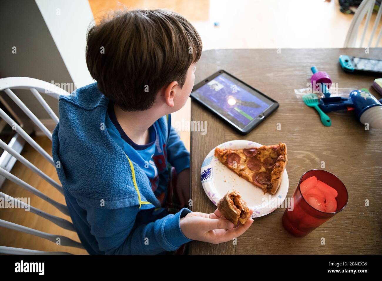 Overhead View of Teen Boy With Flu Eating Pizza Watching Ipad at Table ...