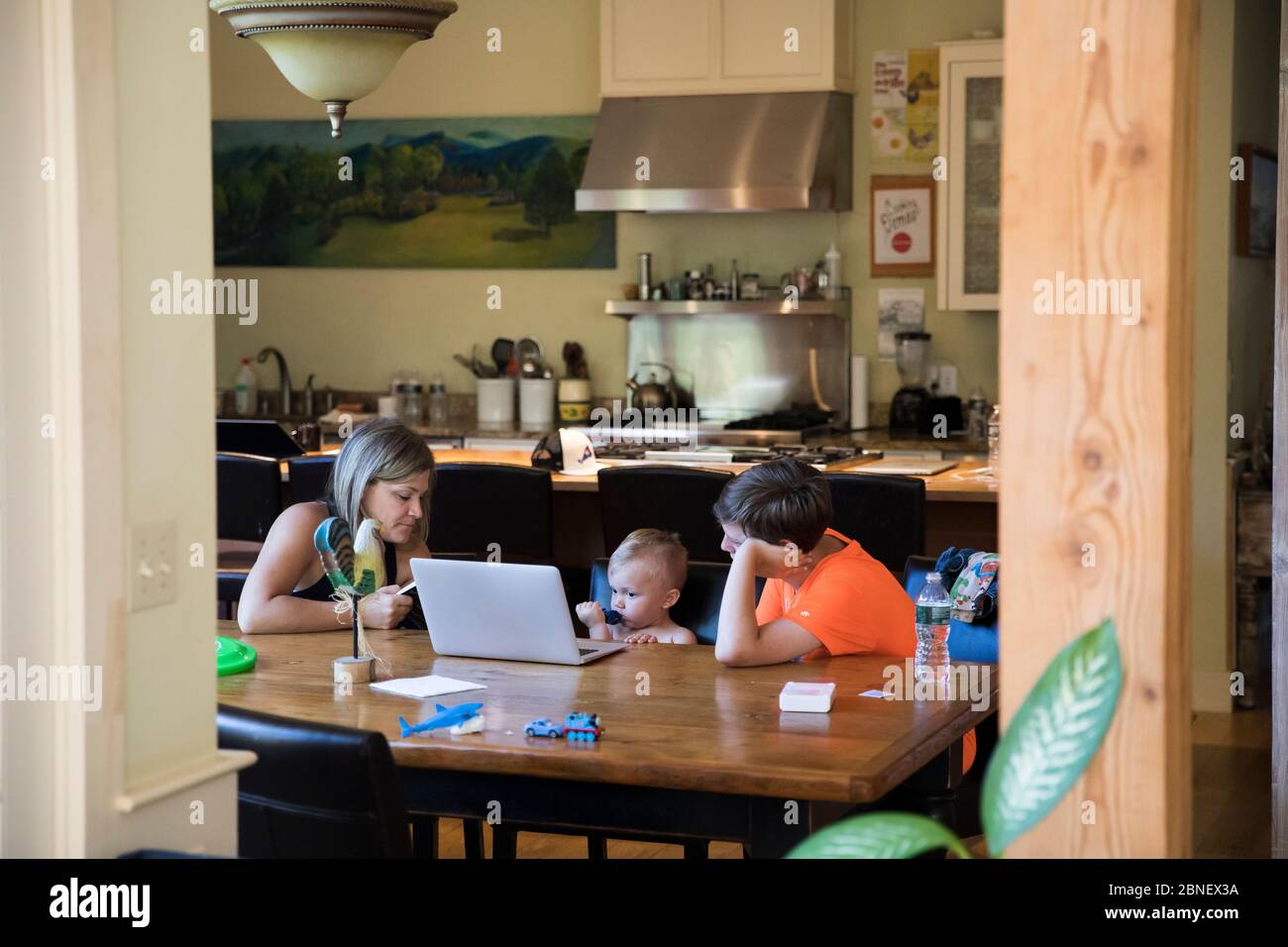 Wide View of Mom at Table With Toddler Son on Laptop and Teen Cousin ...