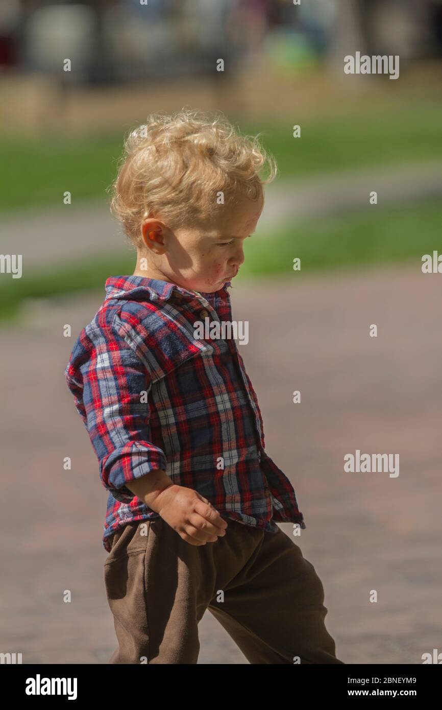 Cute shot of blonde, curly haired child, walking. Face is messy with ...