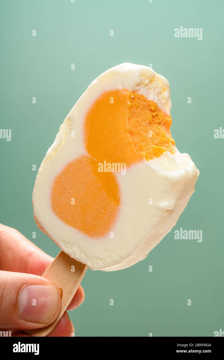 hand holding egg shape popsicle with a bite on green background Stock ...