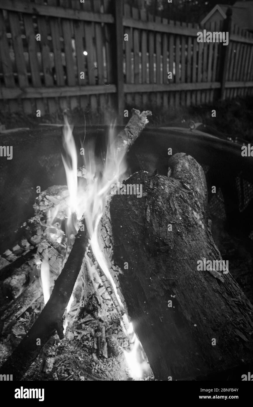 Vertical greyscale shot of fire captured in a backyard next to a wooden ...