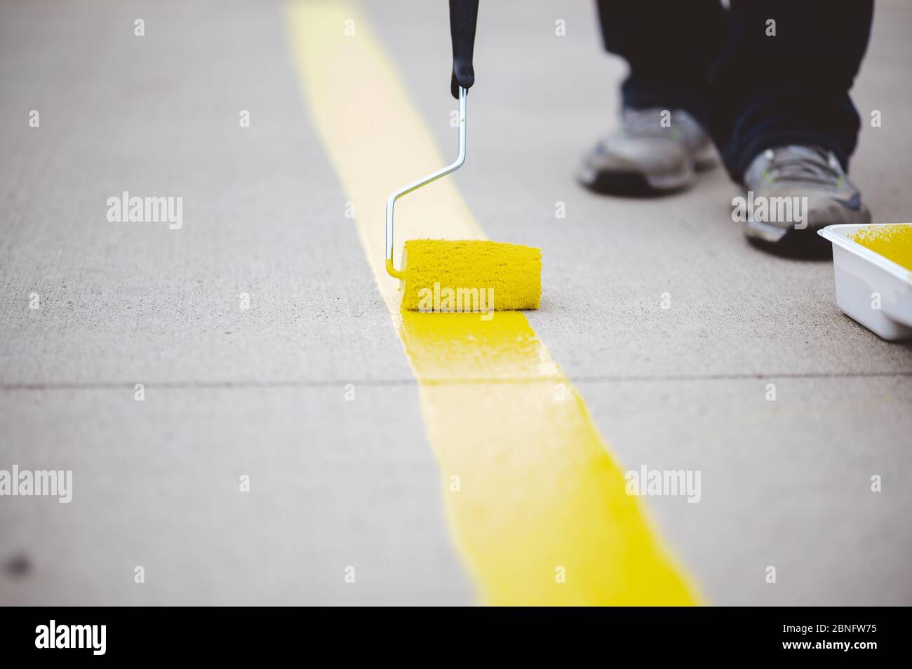 Man painting a yellow line on concrete ground using a roller Stock ...