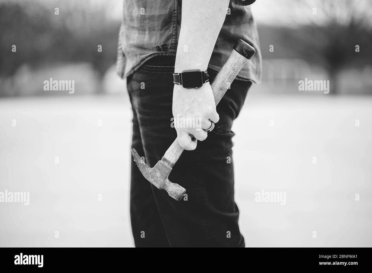Man in jeans holding an old rusty hammer in grayscale Stock Photo - Alamy