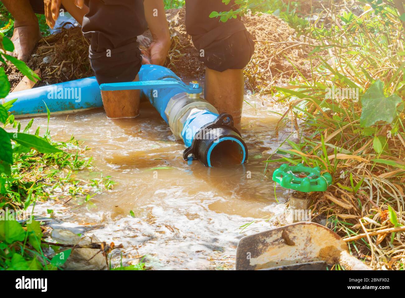 broken pipe in hole with water motion at roadside and plumber working ...