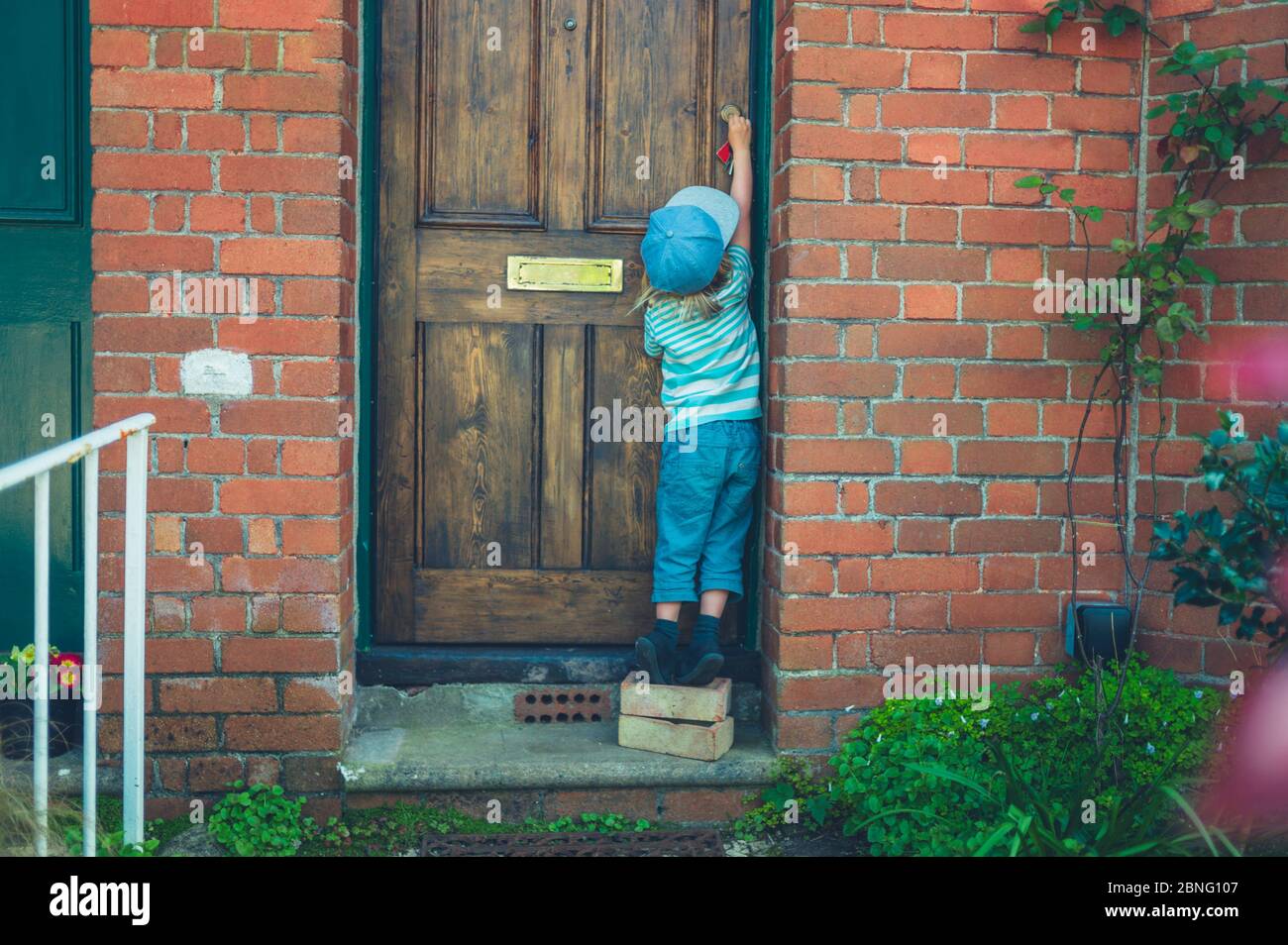 A little preschooler is standing on some brick to unlock the front door ...
