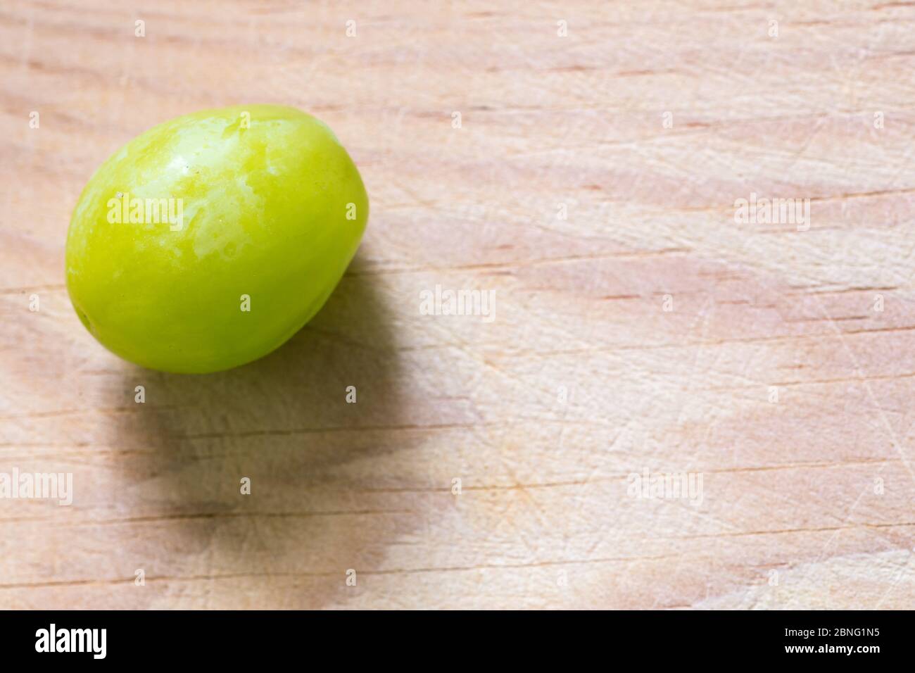 A yellow grape cut in two on a wooden board illuminated with natural ...