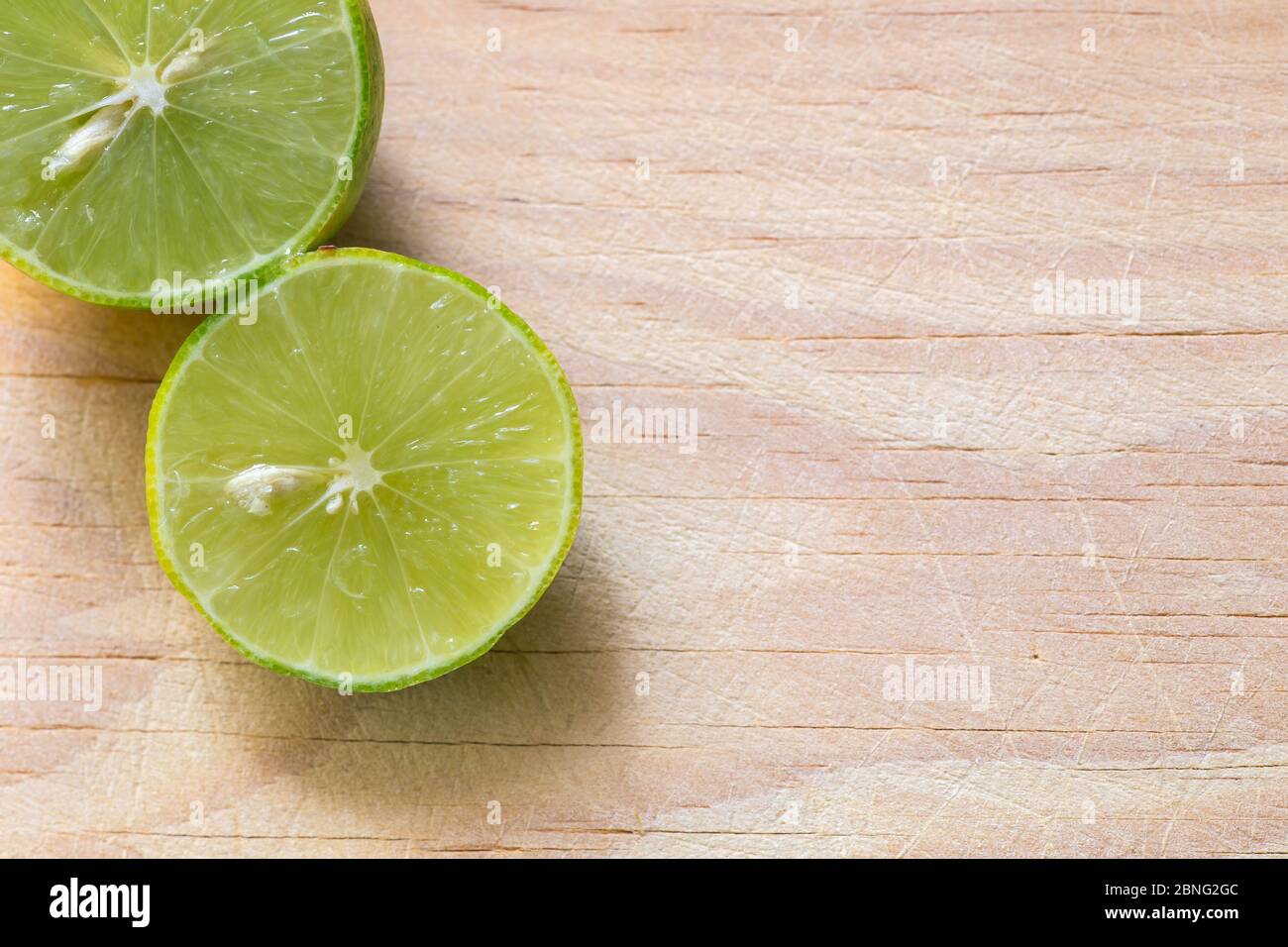 This photograph of a juicy green lemon cut in half on a wooden board ...