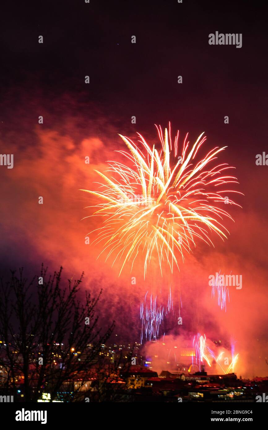Vertical shot of colorful fireworks above a city with lights at night ...