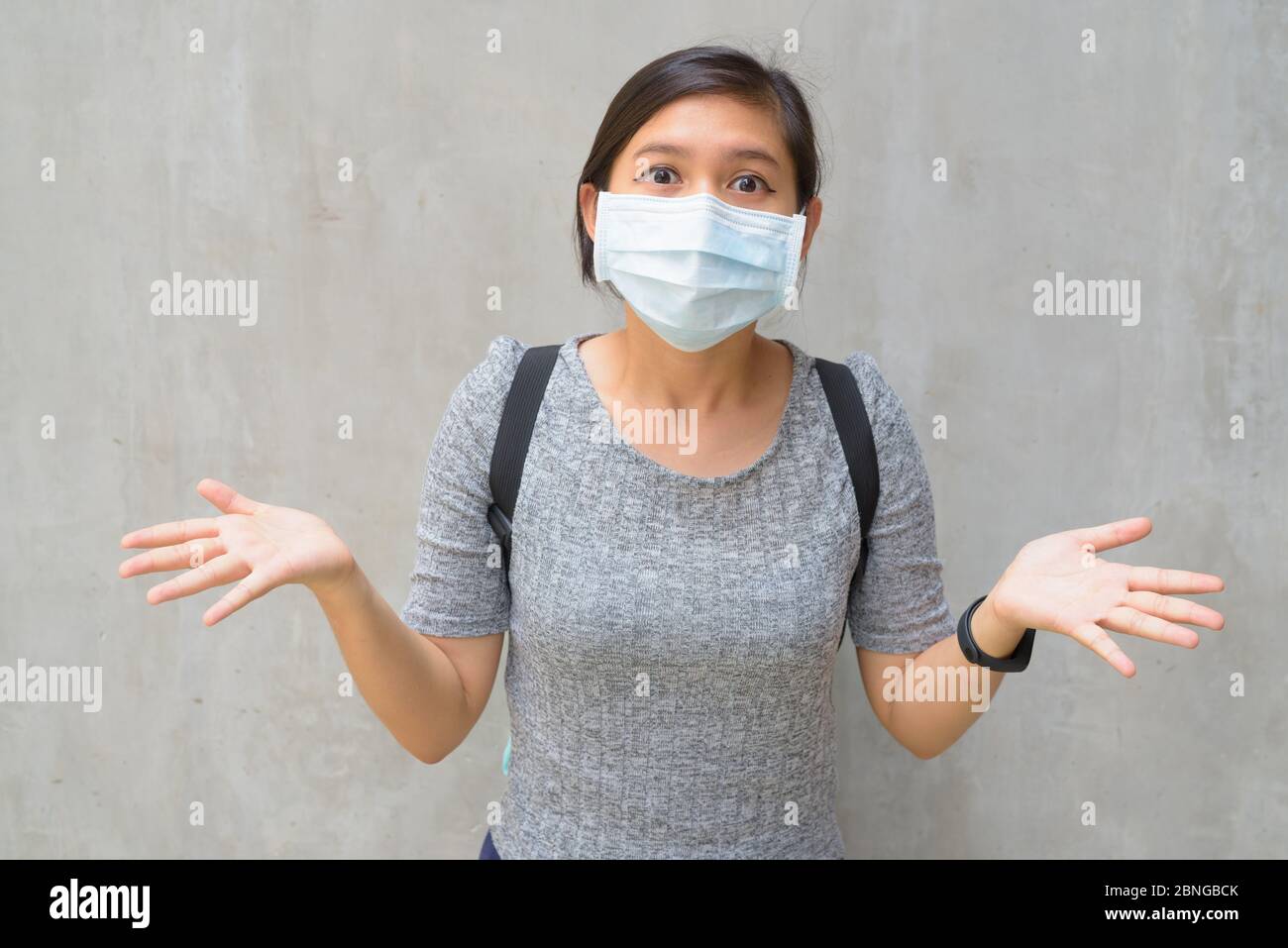 Confused young Asian woman with mask shrugging shoulders outdoors Stock ...