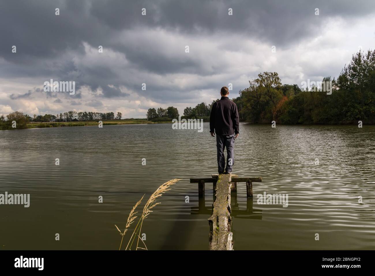 Young man standing on water gate on small pond at fall with dramatic ...