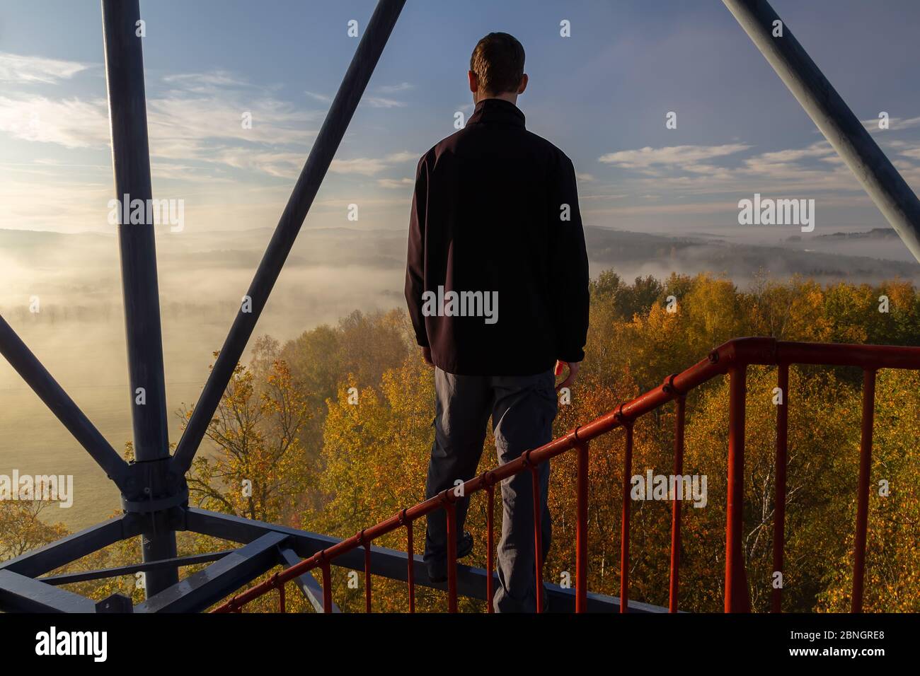 Young man standing on watchtower construction looking to autumn foliage ...