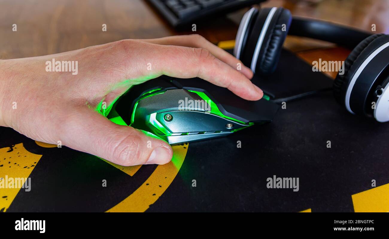 Man hand holding green gaming mouse on pad with headphones and keyboard ...