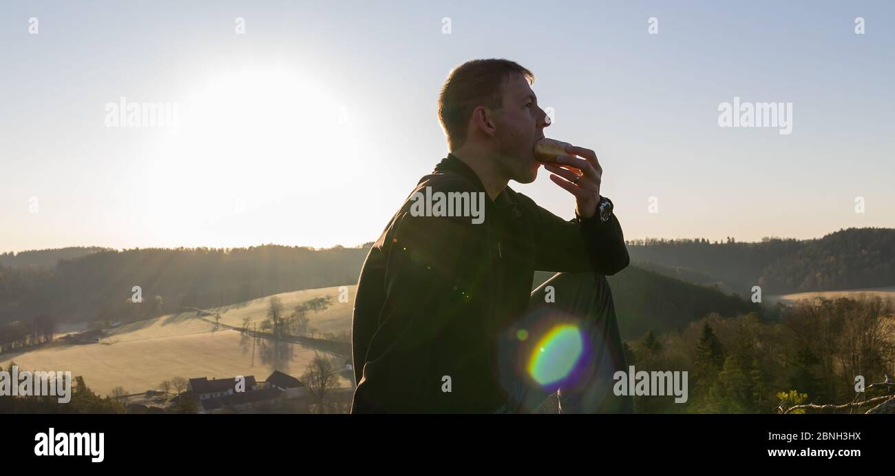 Young caucasian man enjoy eating morning breakfast donut on rock with ...