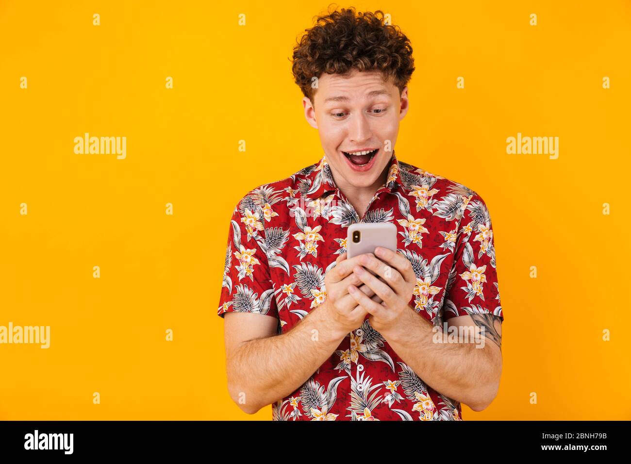 Image of young delighted man using cellphone and expressing surprise ...