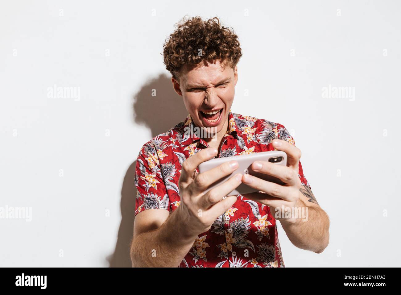 Image of young delighted man playing video game on cellphone and ...