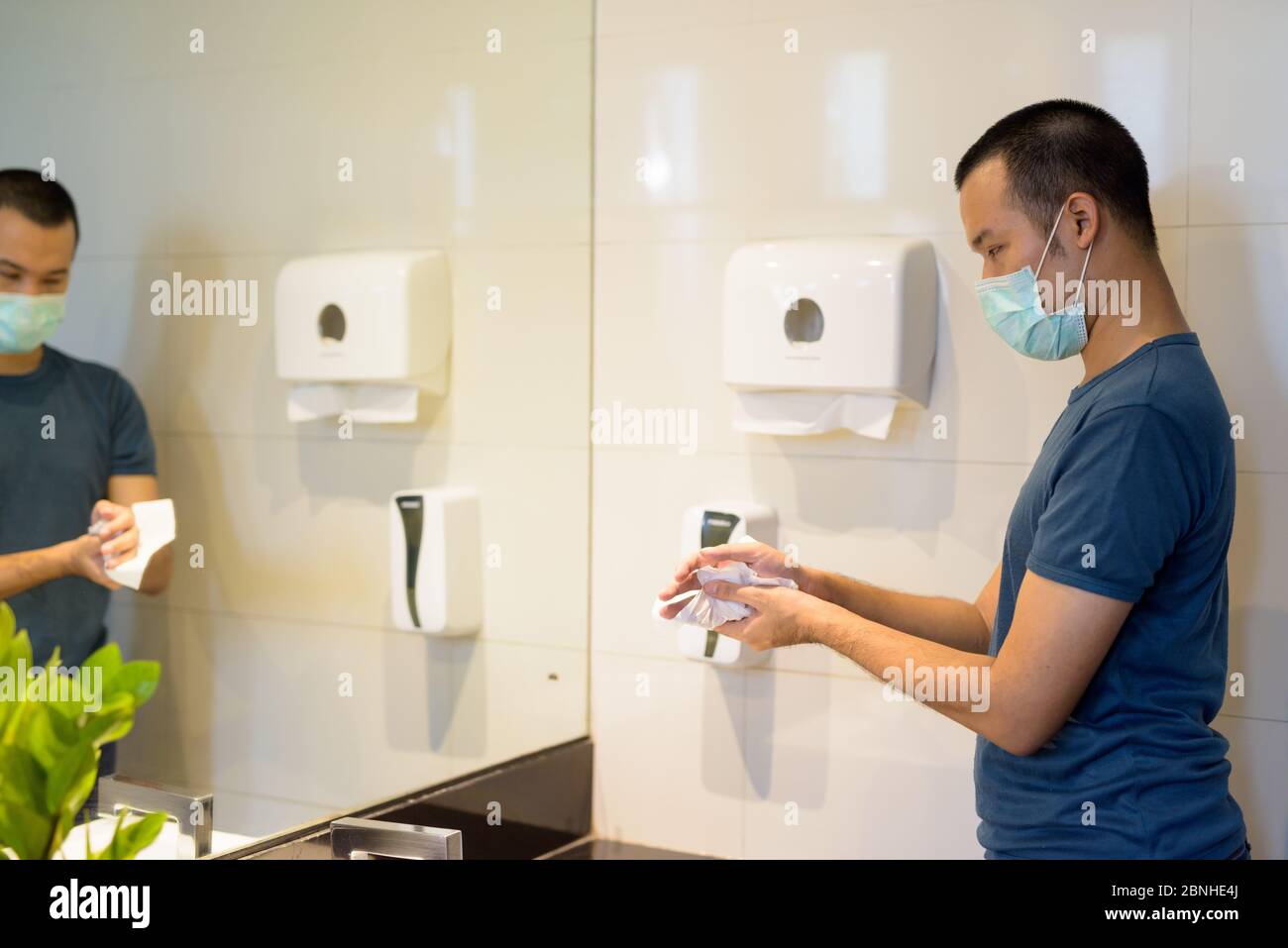 Young Asian man wearing mask and drying hands properly with tissue in ...