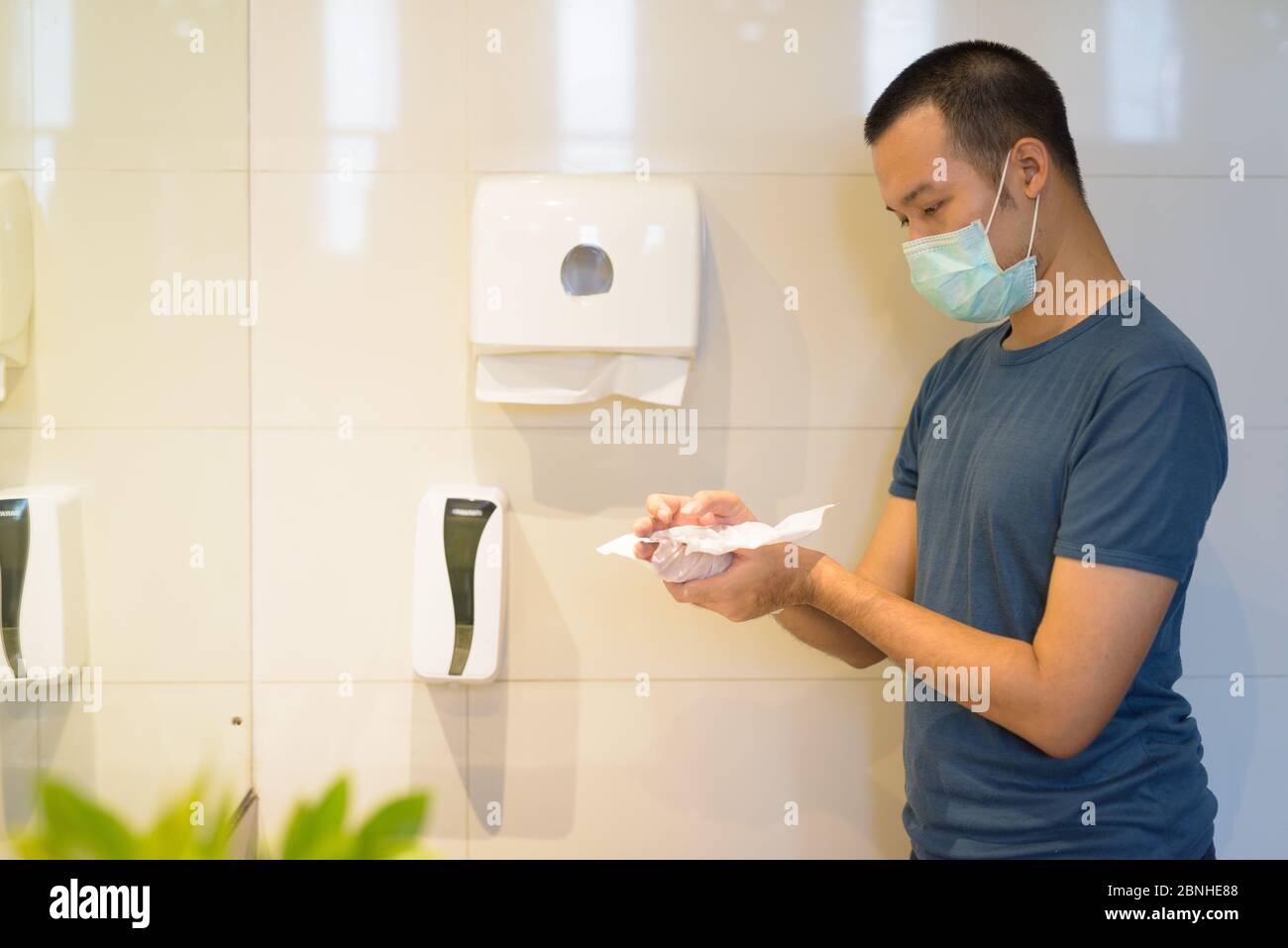 Young Asian man wearing mask and drying hands properly with tissue in ...