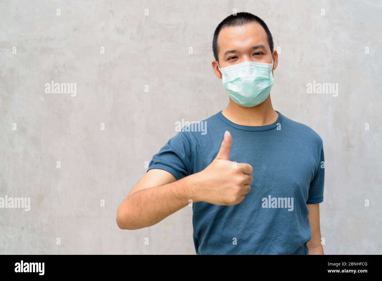 Young Asian man giving thumbs up with mask for protection from corona ...