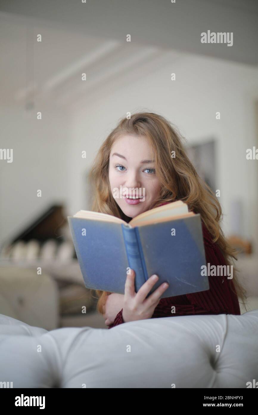 Vertical shot of a beautiful young blonde female reading a book with an ...